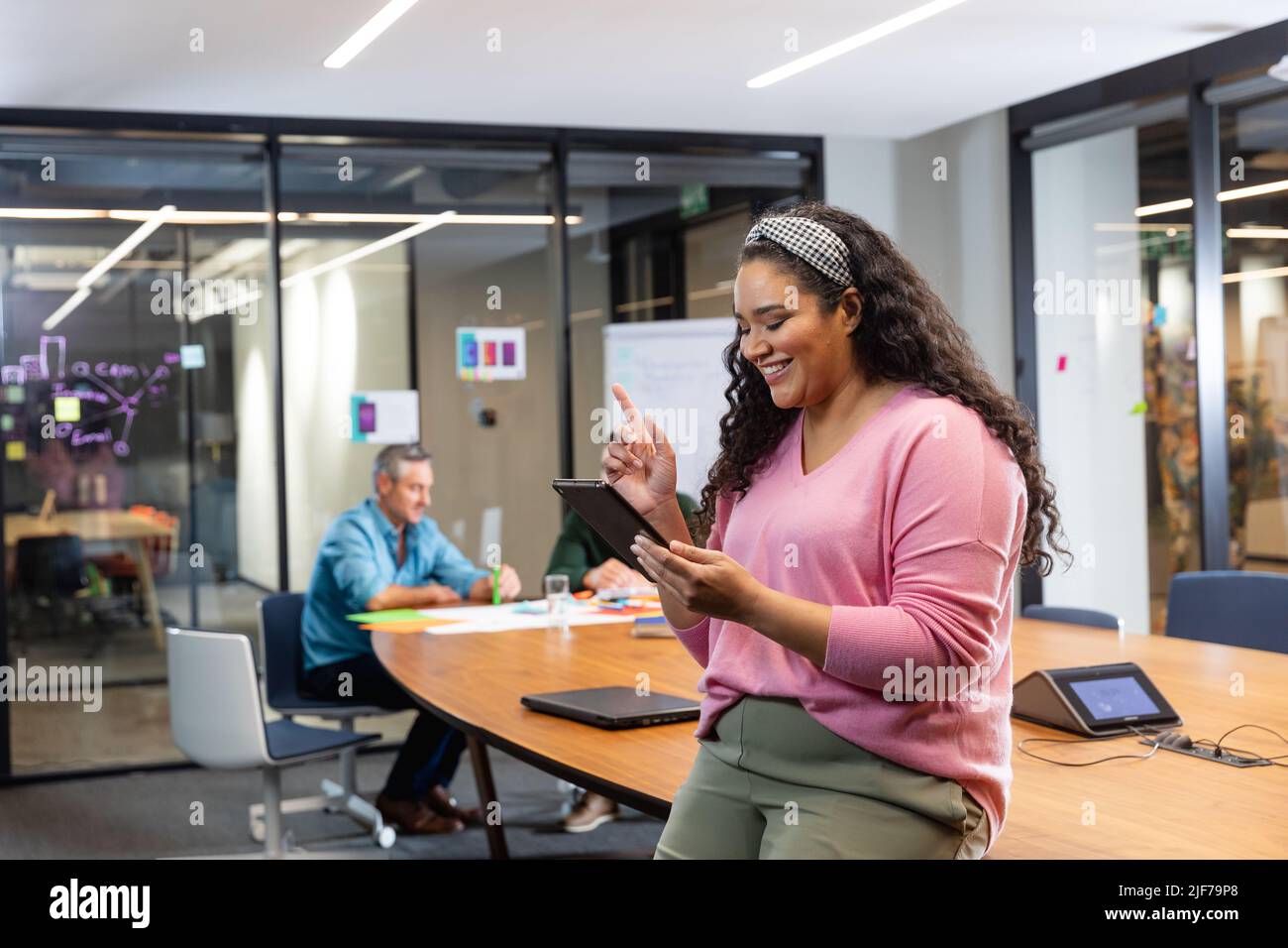 Smiling young biracial businesswoman using tablet pc while colleagues ...