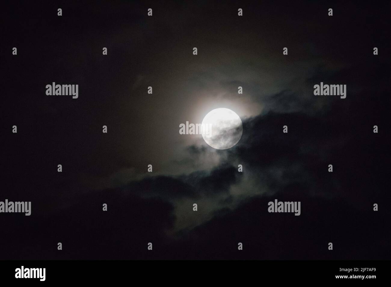 A shot of the full Moon behind clouds at night Stock Photo - Alamy
