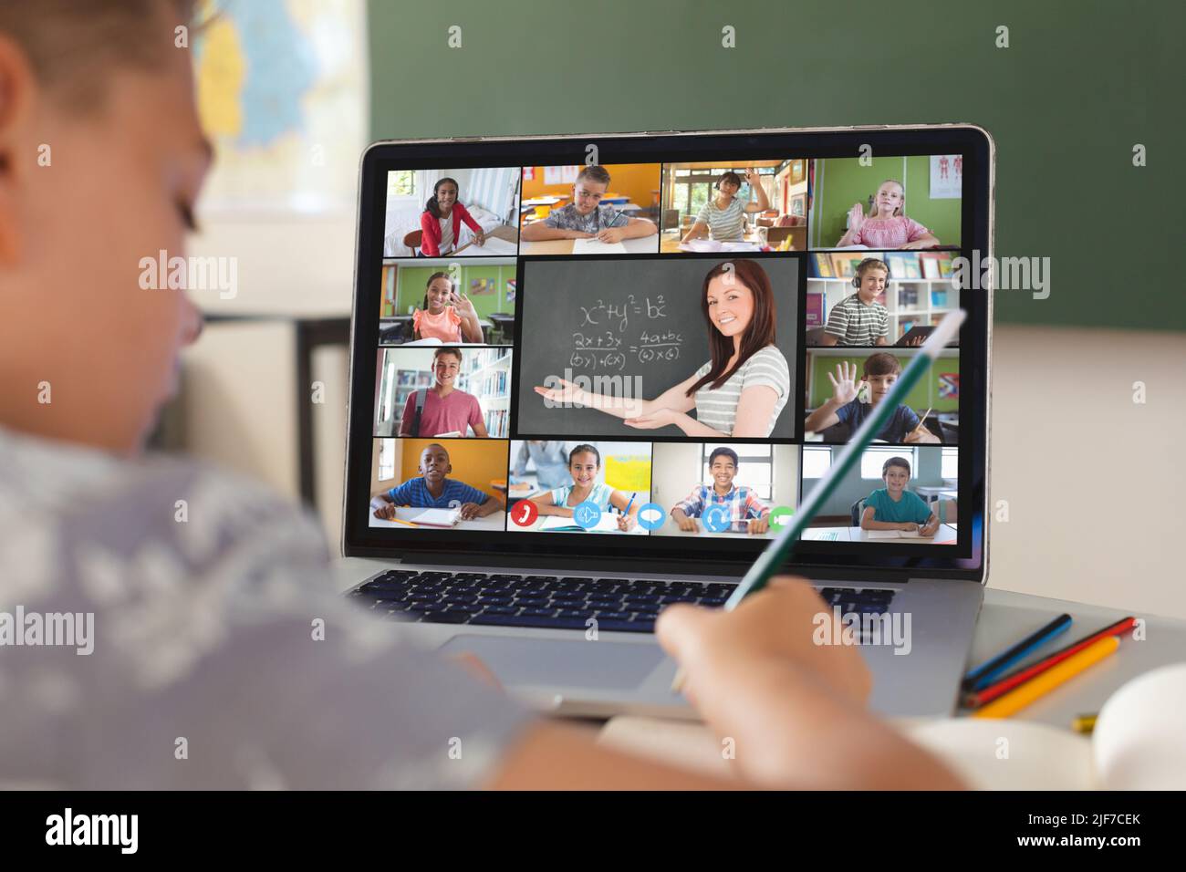 Multiracial boy writing while attending online class with teacher and ...