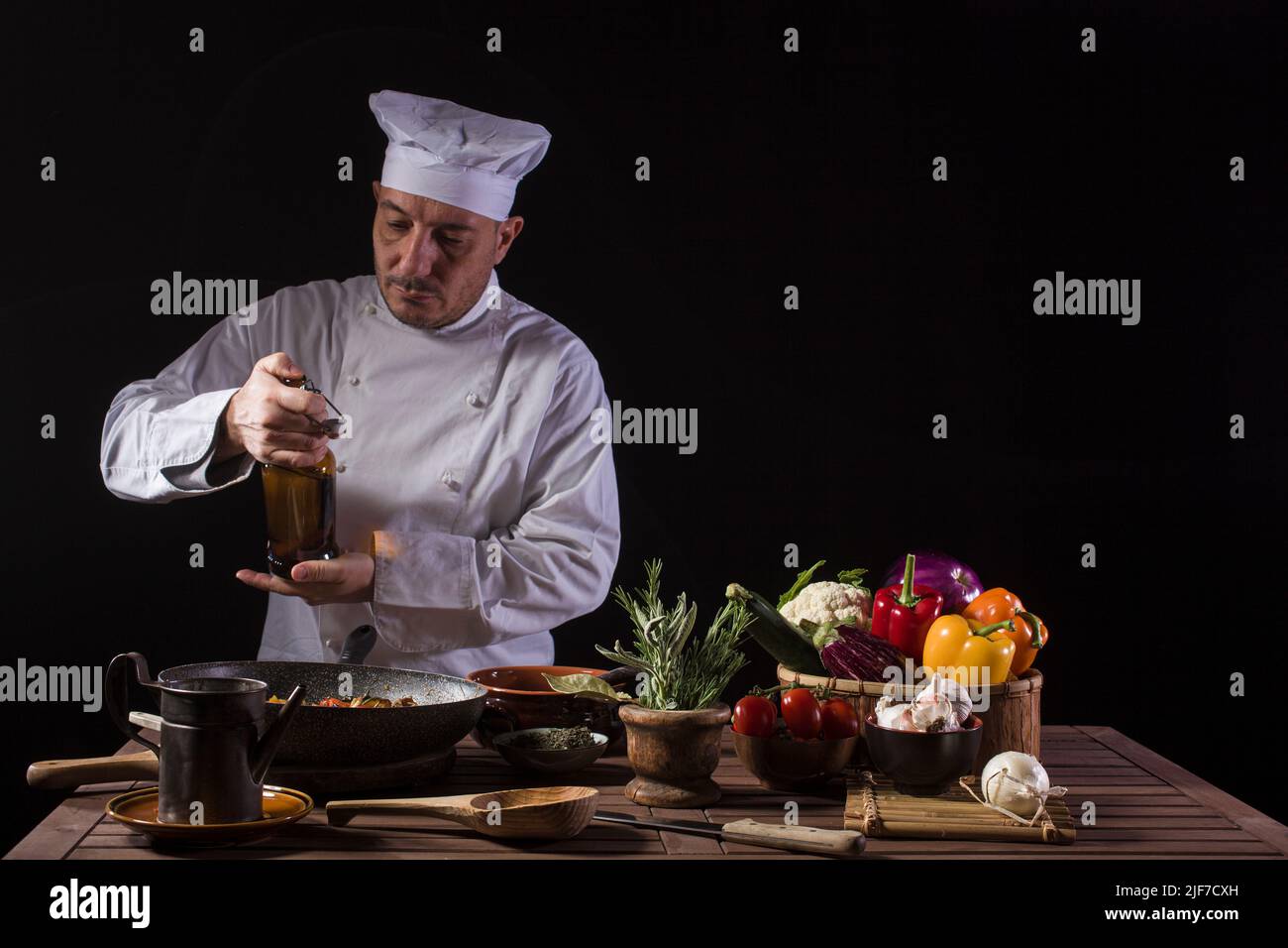 Male chef in white uniform ready to pouring vinegar onto the cooking ...