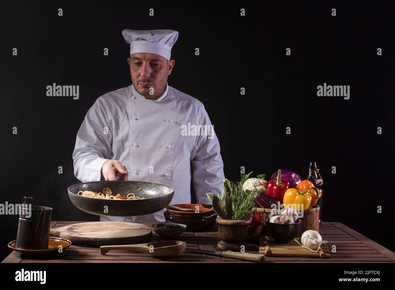 Male chef in white uniform holding a frying pan, sautéing spaghetti ...