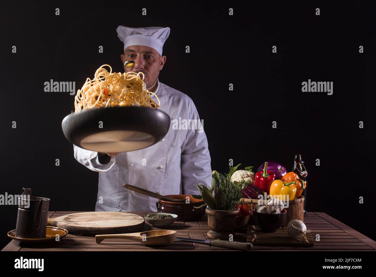 Male chef in white uniform holding a frying pan, sautéing spaghetti ...