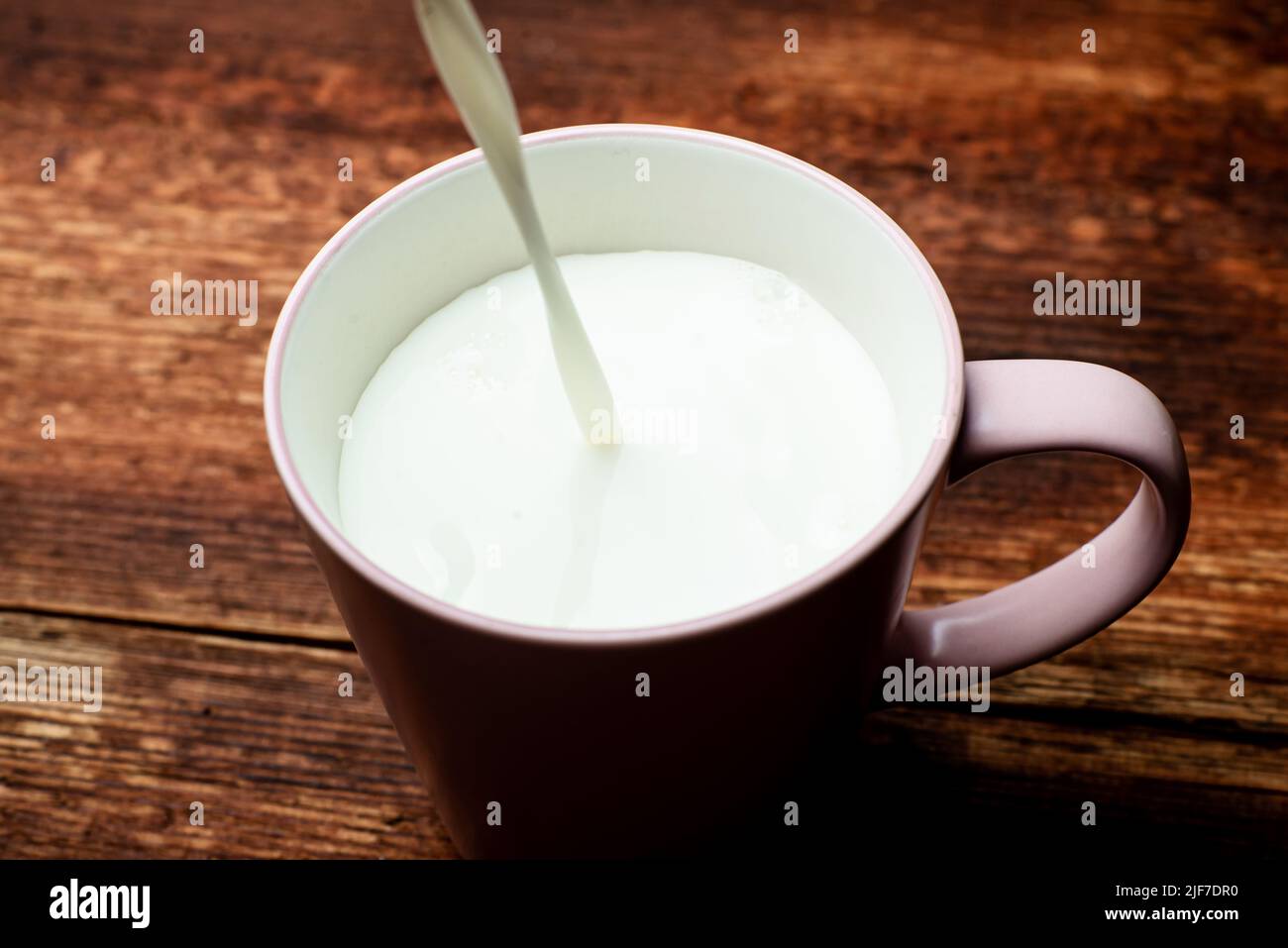 Milk is poured into a cup on a brown wooden background Stock Photo - Alamy