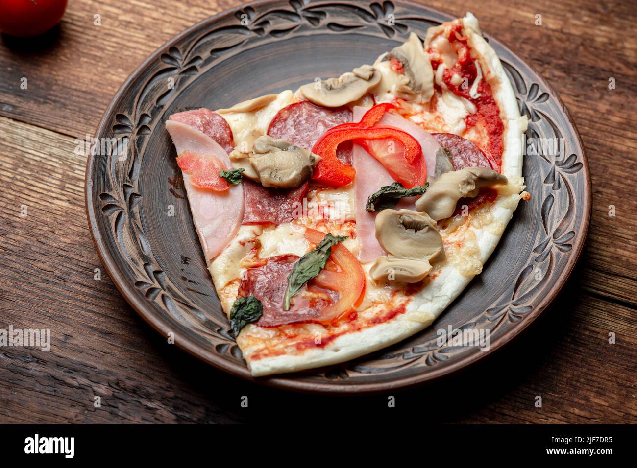 Pizza with ham and bacon, mushrooms on a clay plate on a brown wooden ...