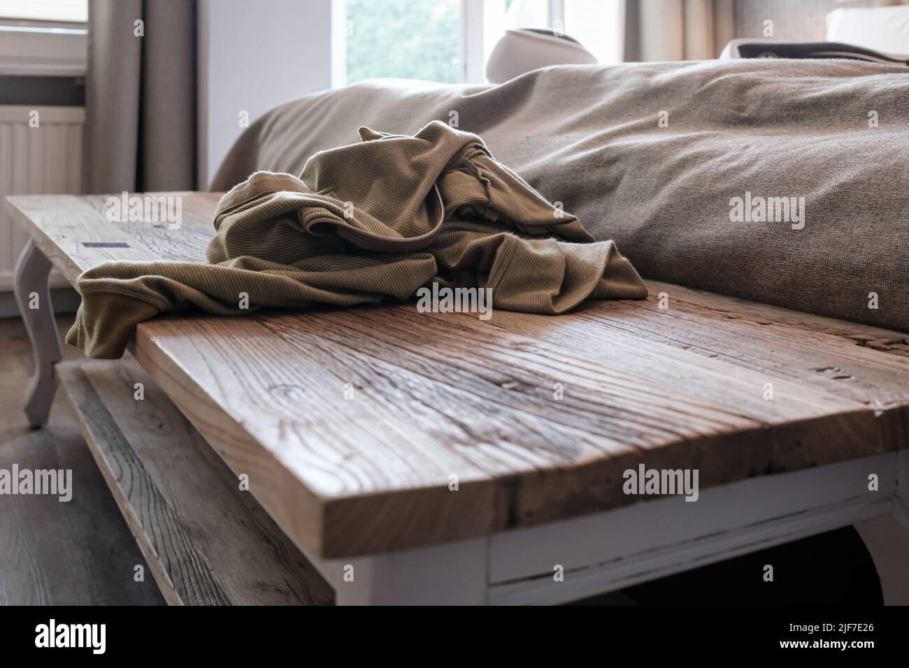 Bedside wooden table on which clothes are casually thrown, in the ...