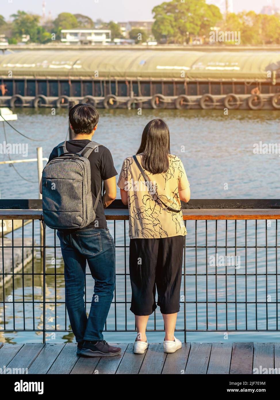 Back view of Asian couple relaxing and chilling at a riverside. Relaxed ...