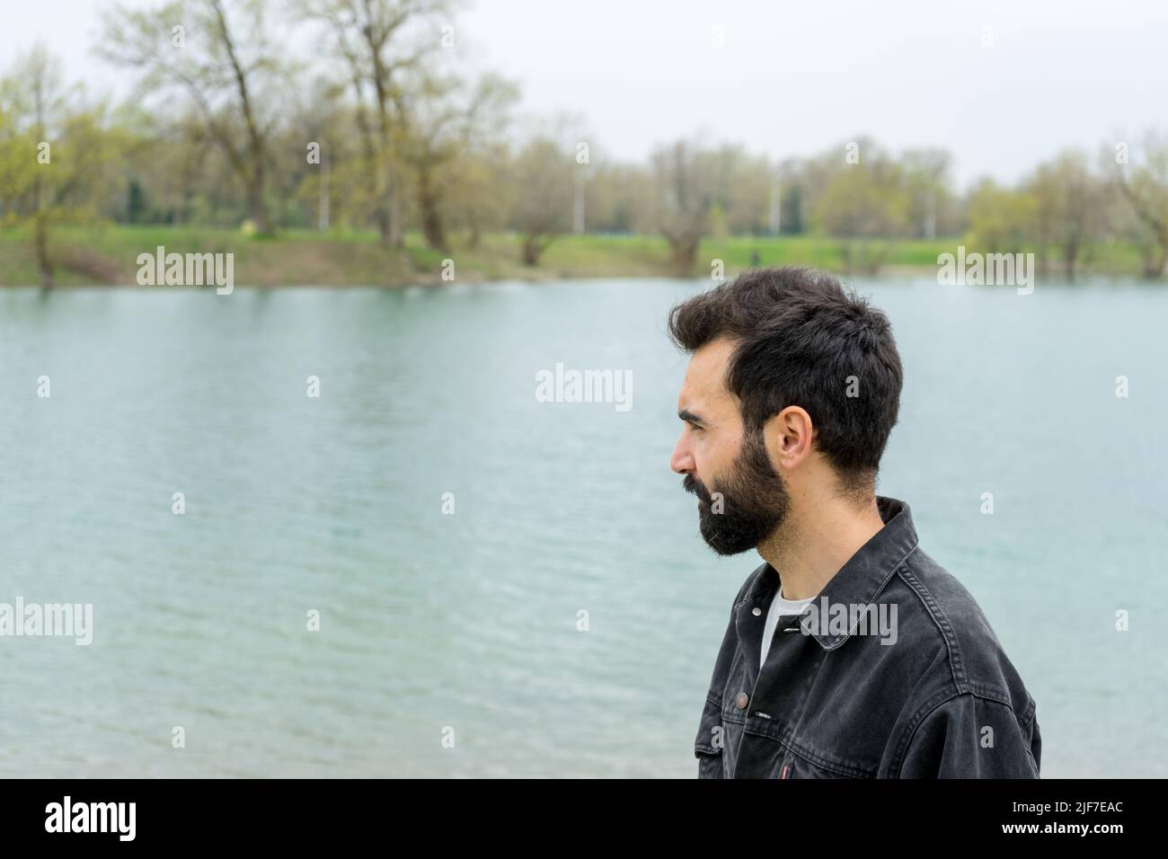 A young Caucasian beard man looking sad in front of a blue lake Stock ...