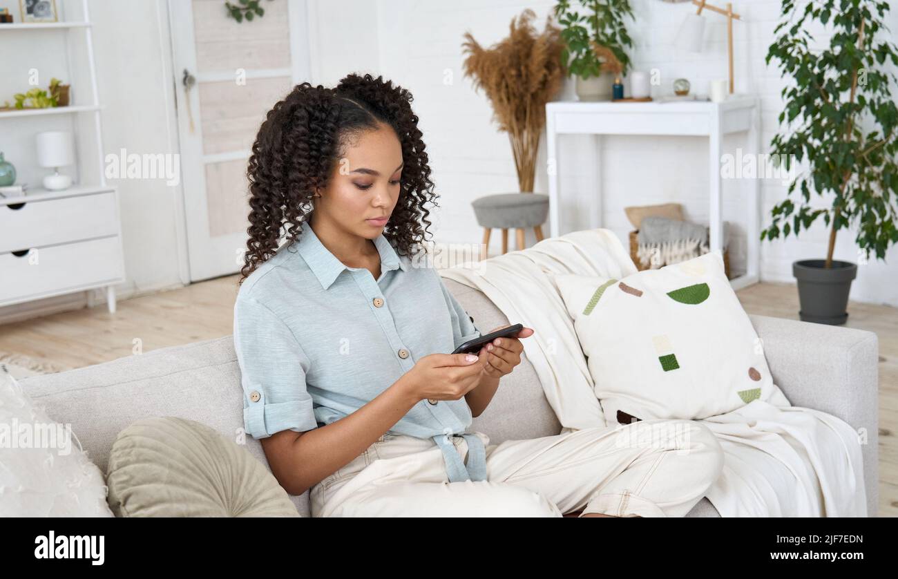 Young Afro American woman sitting sofa using cell phone at home Stock ...