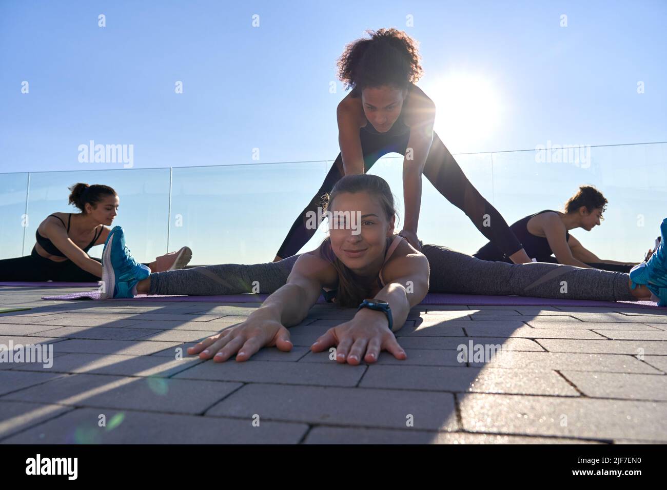 African instructor helps flexible caucasian woman at group yoga class ...