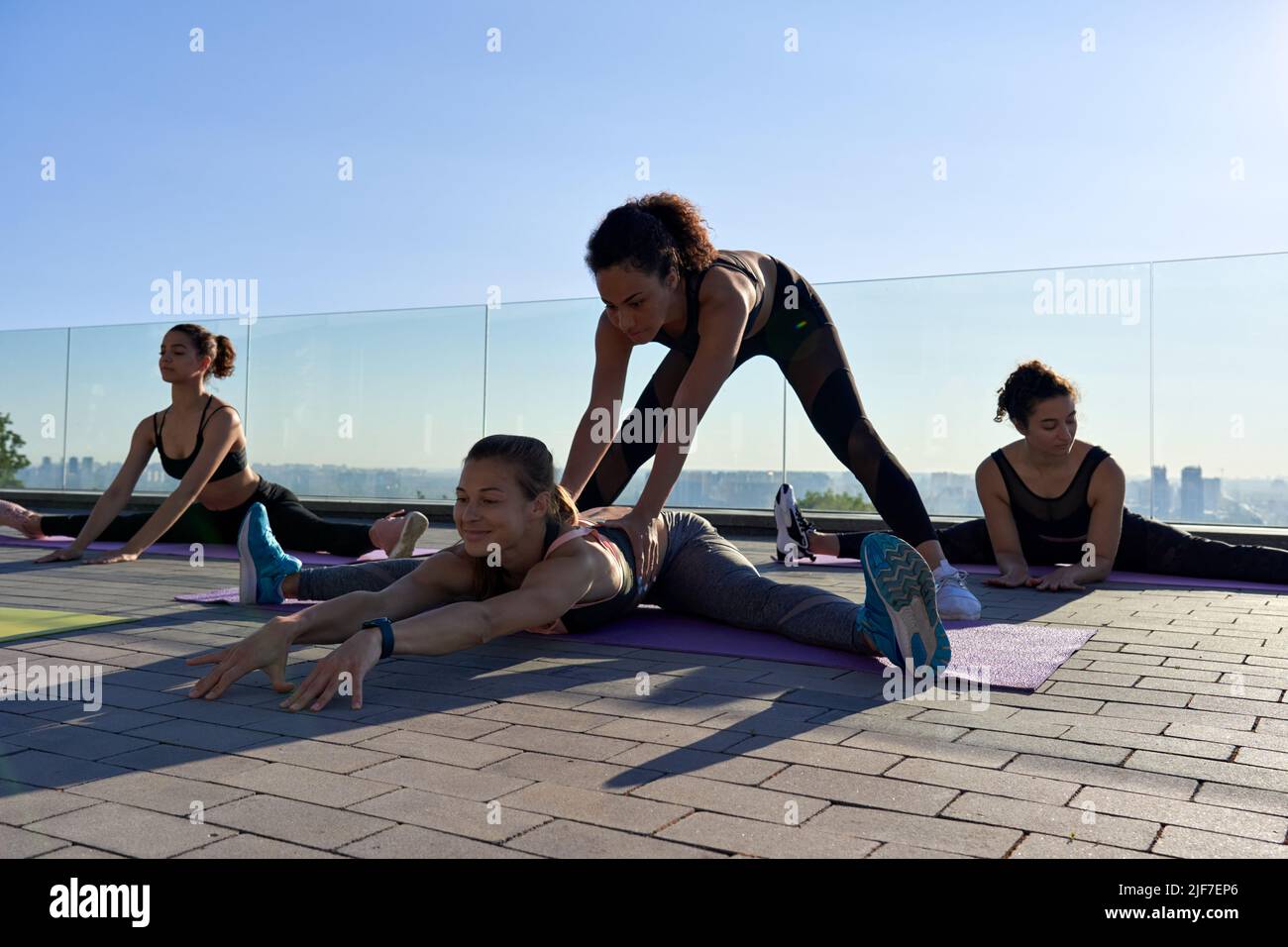 Fit african coach helping flexible caucasian woman at group yoga class ...