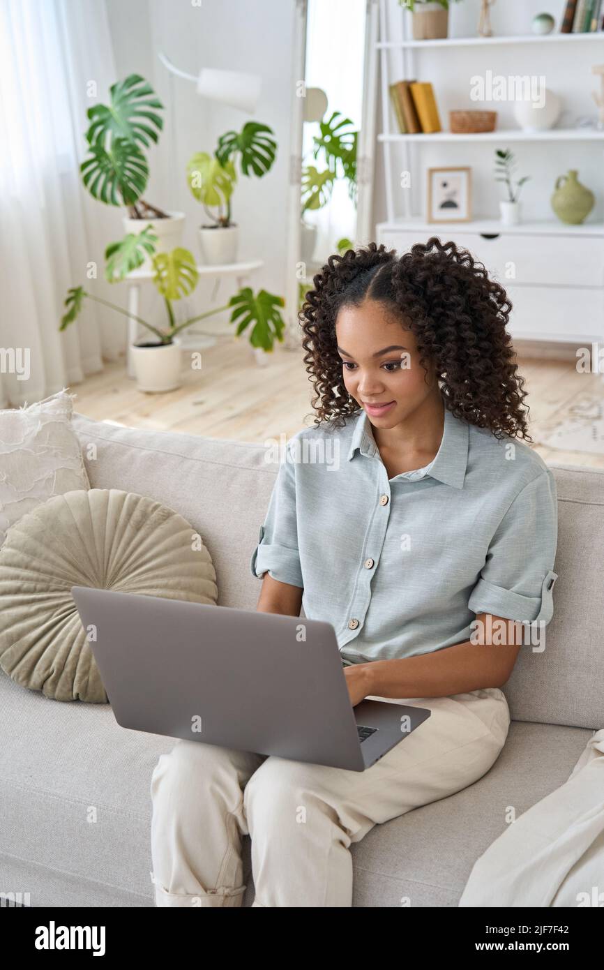 Happy African American teen girl using laptop computer sitting on sofa ...