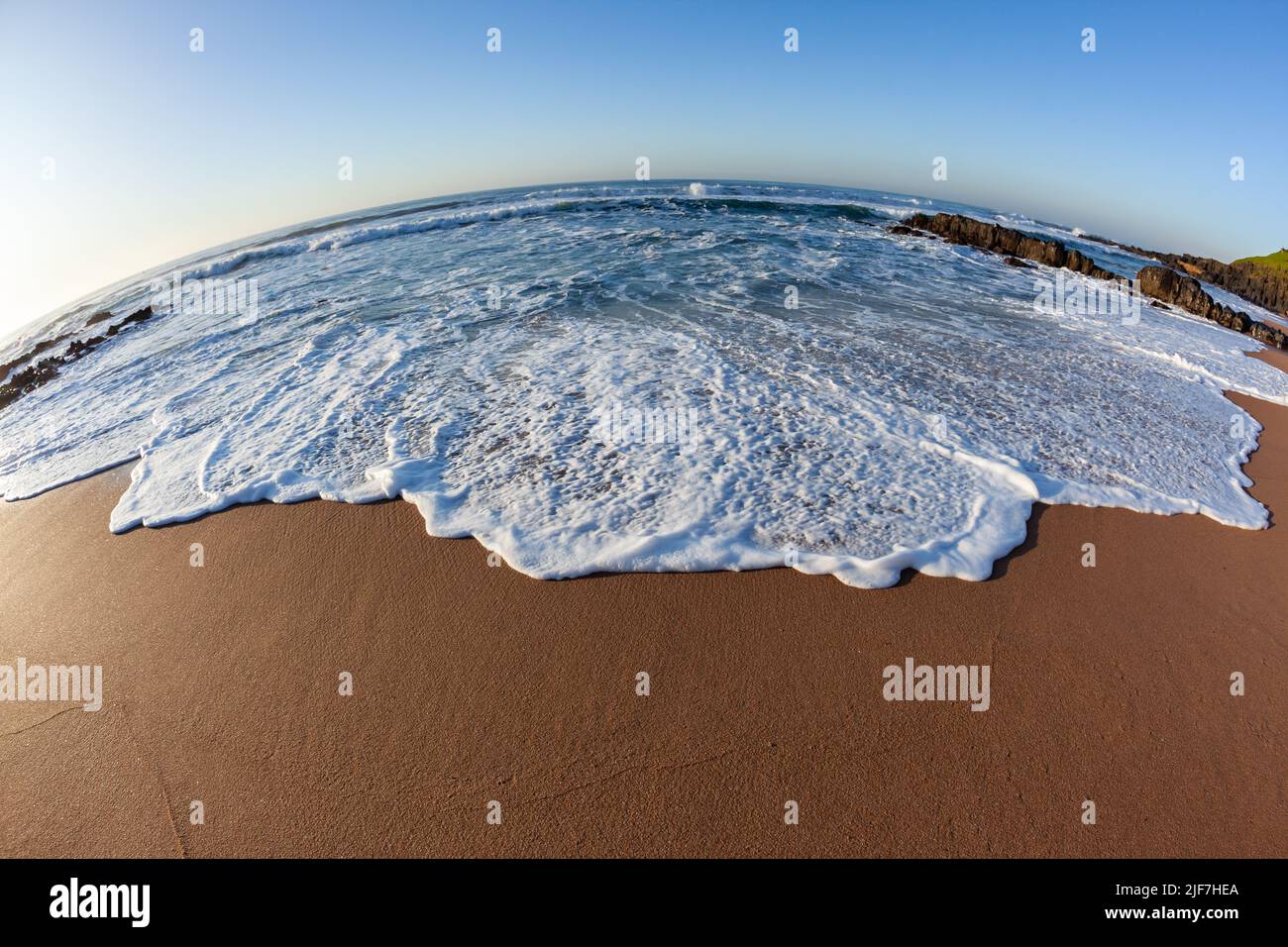 Beach sand waters edge wave wash close up wide angle photo along rocky ...