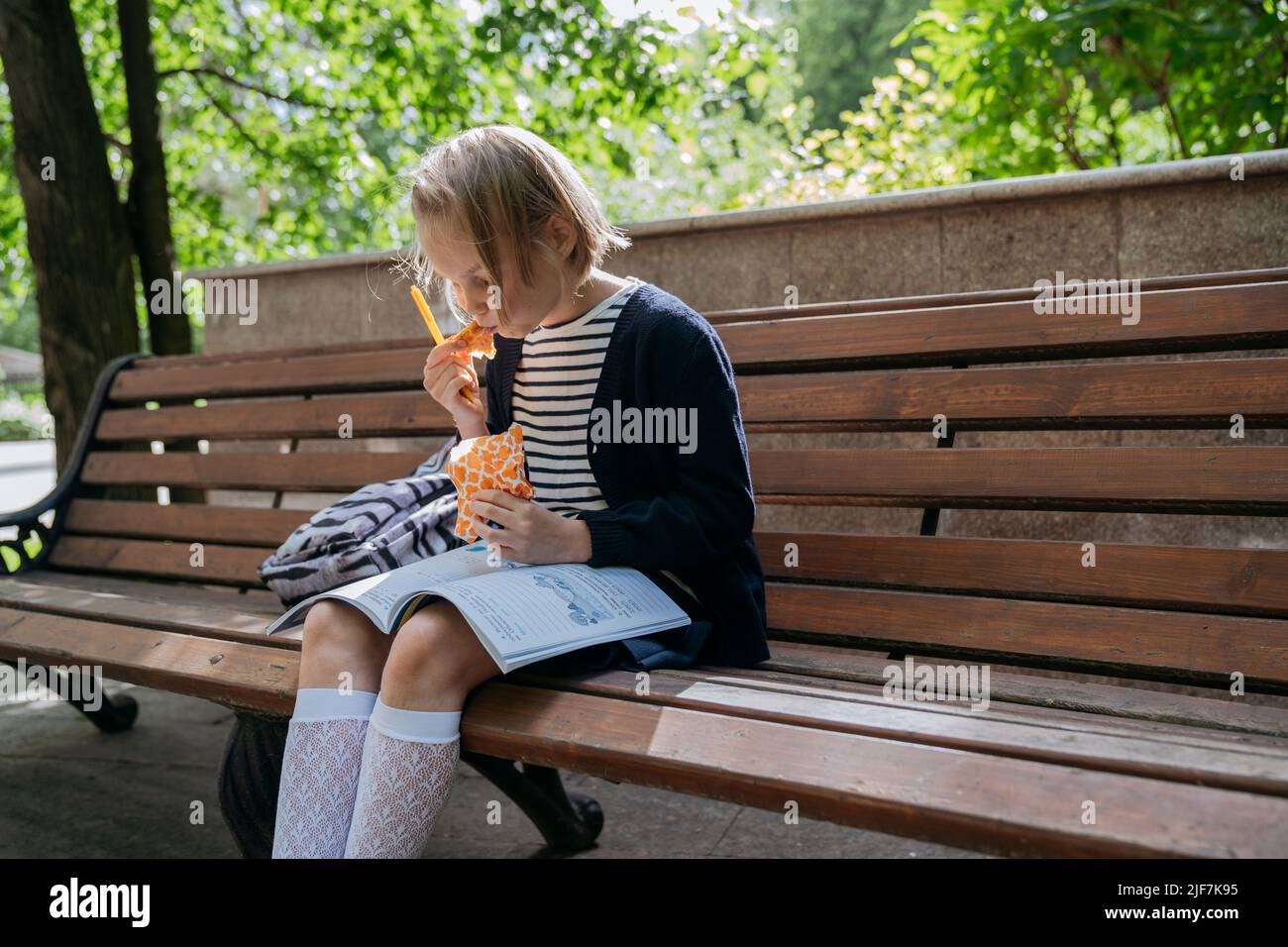 A schoolgirl eats a sandwich and does her homework in the park Stock ...