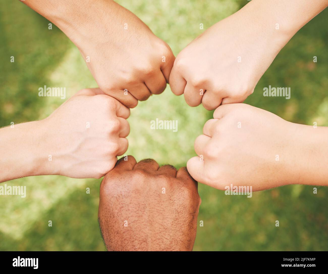 Multiethnic hands fist bumping outside in nature. Closeup of a group of ...