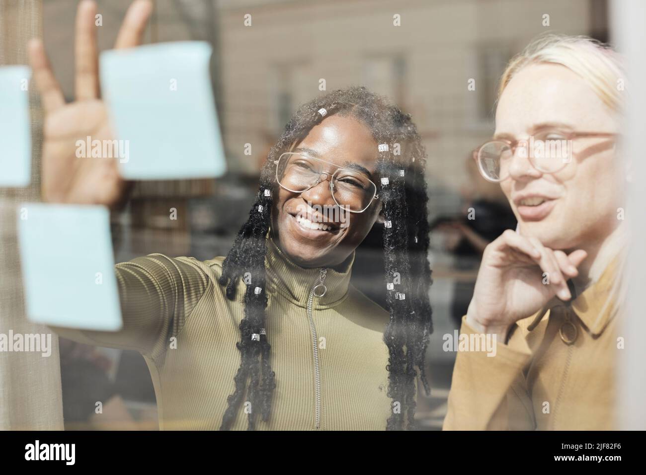 Smiling female entrepreneur explaining strategy to non-binary colleague ...