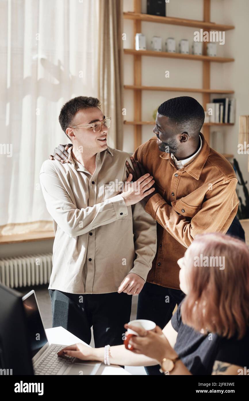 Male computer programmers talking with each other while standing by ...