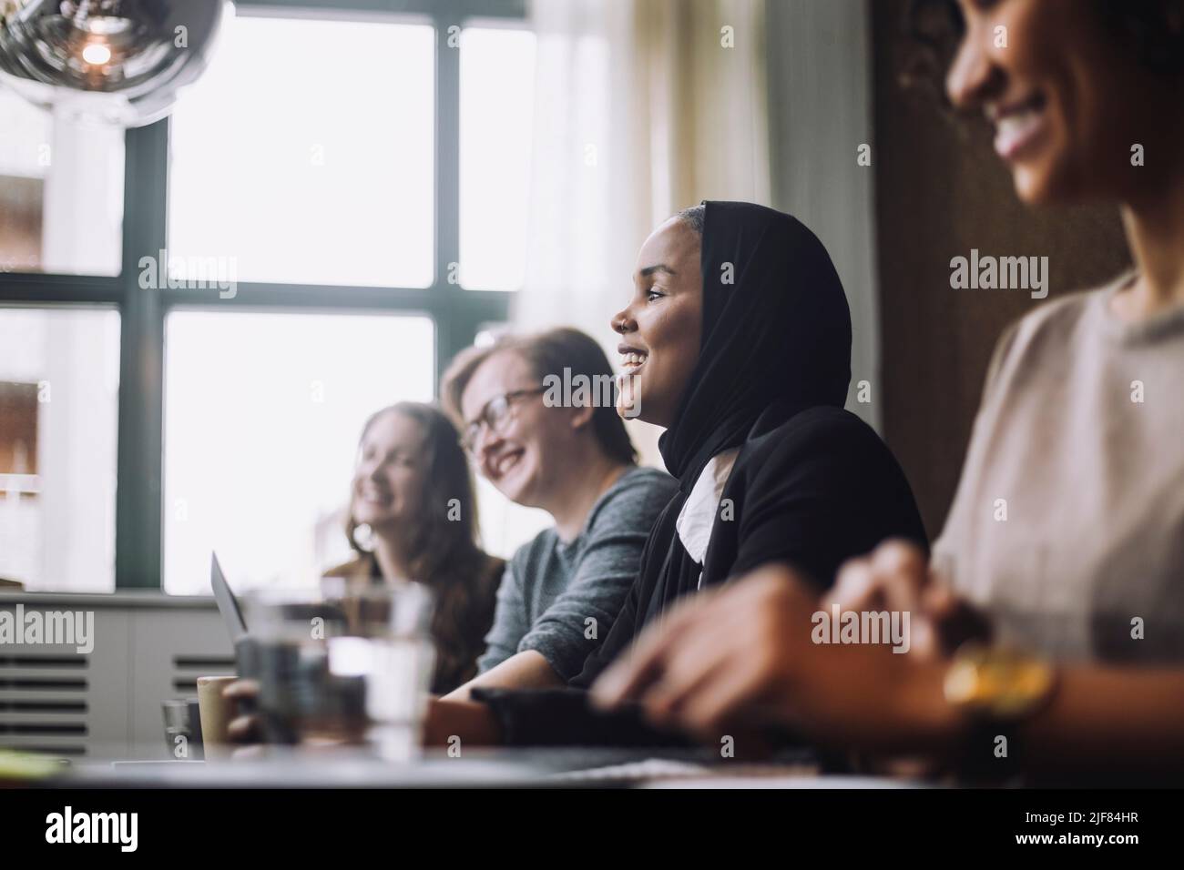 Smiling businesswoman wearing headscarf sitting with colleagues in ...