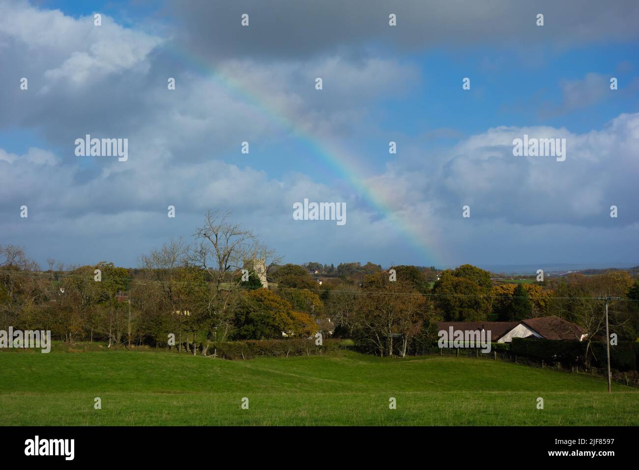 rainbow over Devon village and church with blue sky and clouds Stock ...