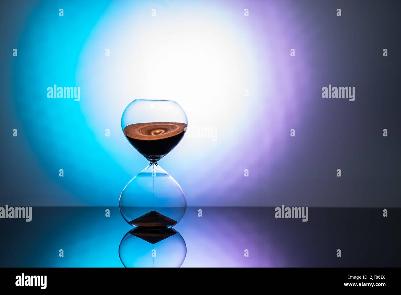 Hourglass standing on mirror surface in neon light Stock Photo - Alamy