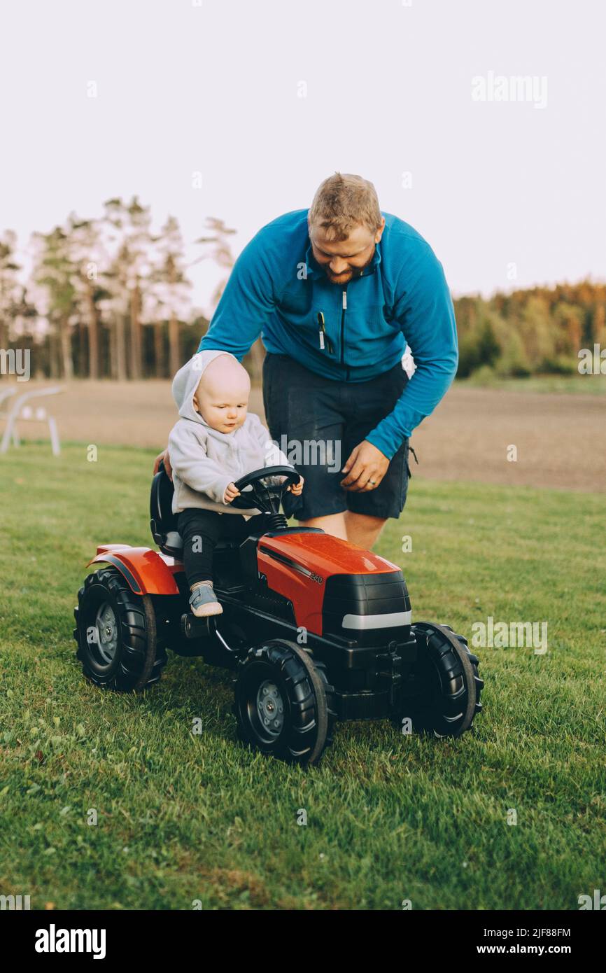 Father giving ride to son sitting in toy tractor at farm Stock Photo ...