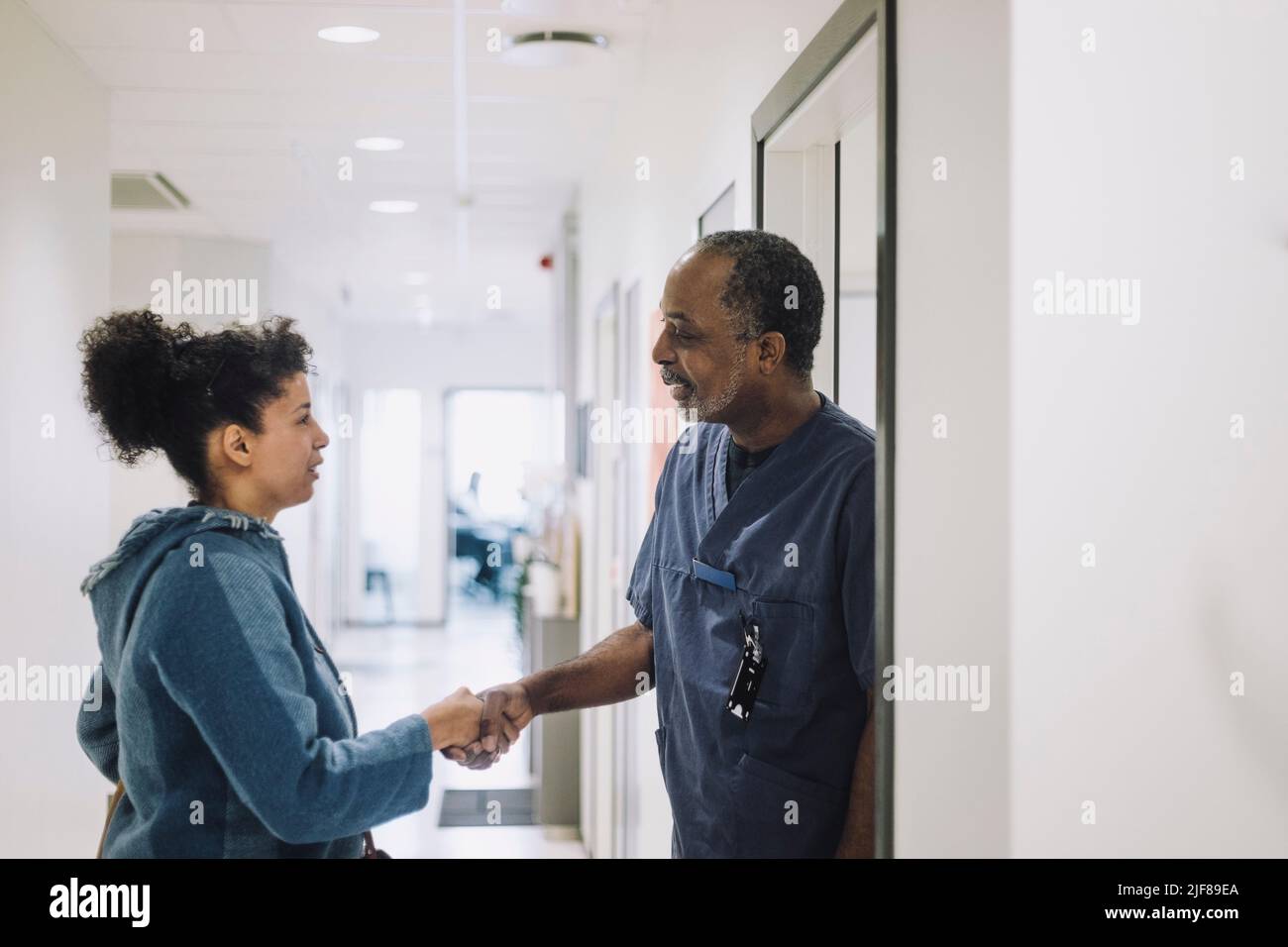 Smiling doctor greeting female patient with handshake while standing at ...
