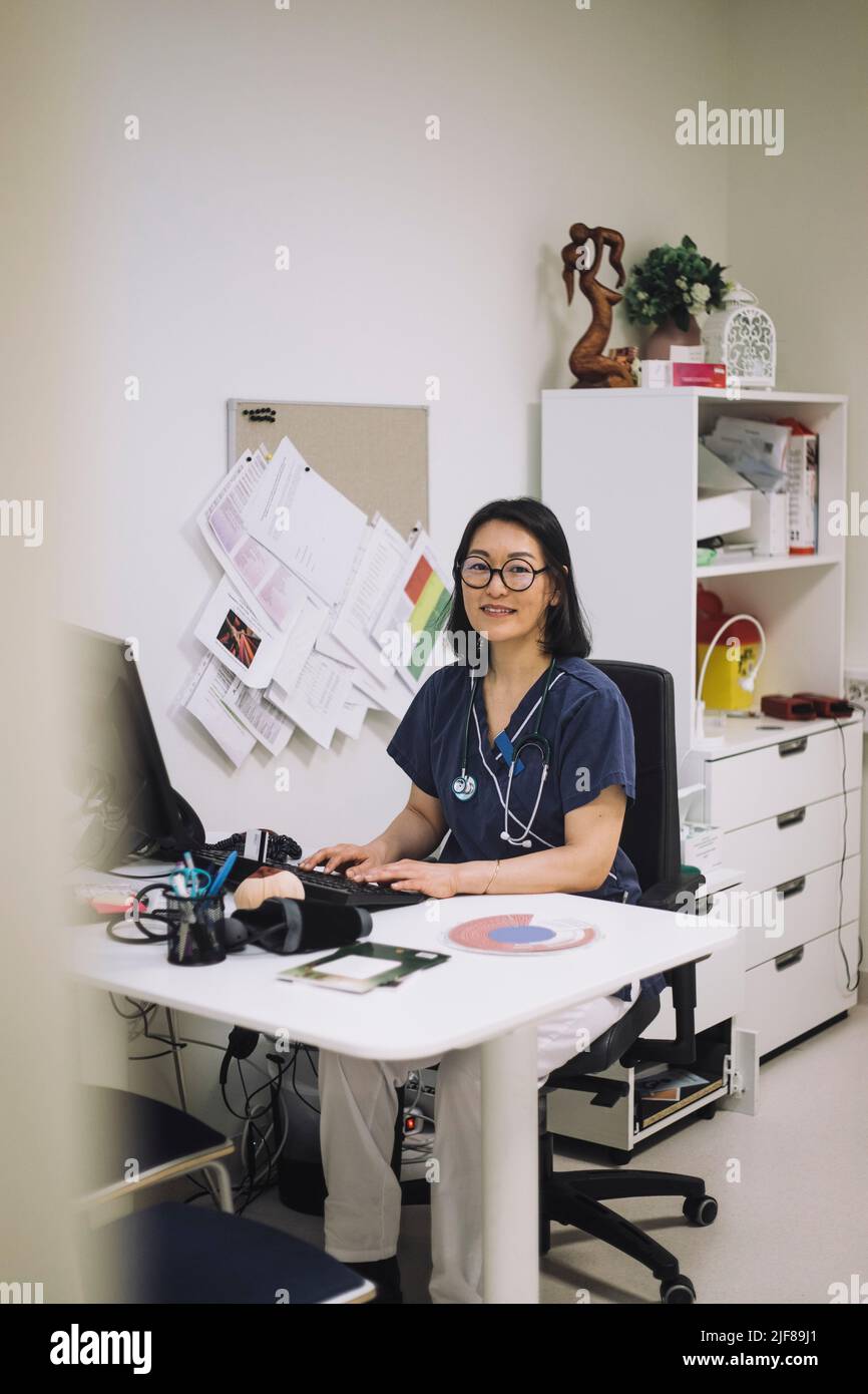 Portrait of smiling female doctor sitting at desk in medical clinic ...