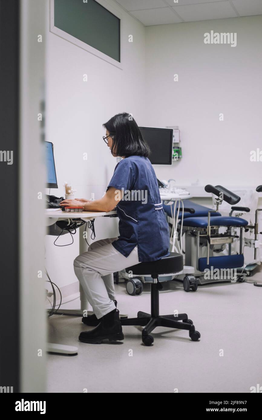Full length of female healthcare expert using computer sitting at desk ...