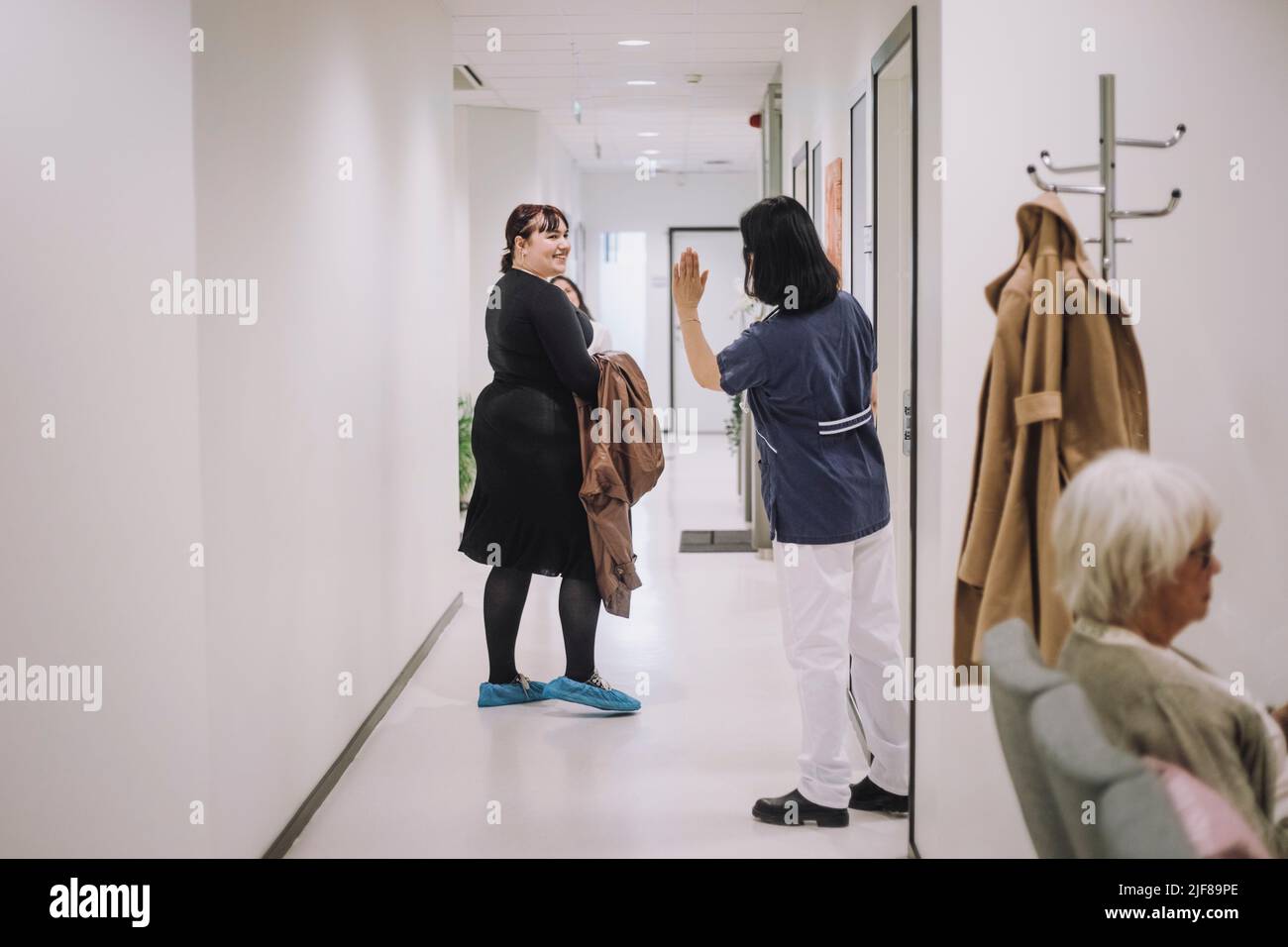 Rear view of female doctor waving at patient leaving medical clinic ...