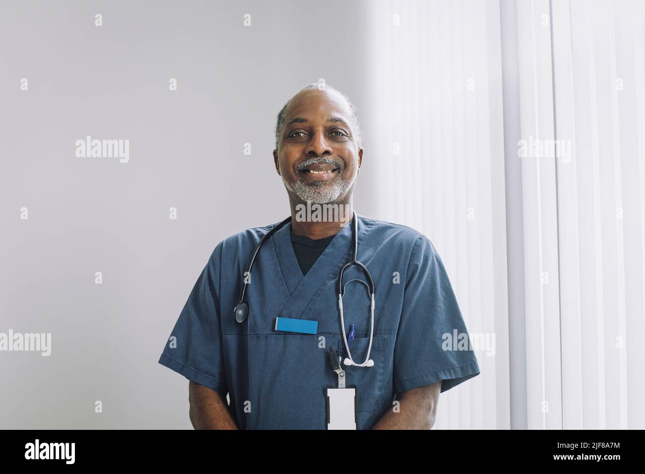 Portrait of smiling male doctor wearing stethoscope standing against ...