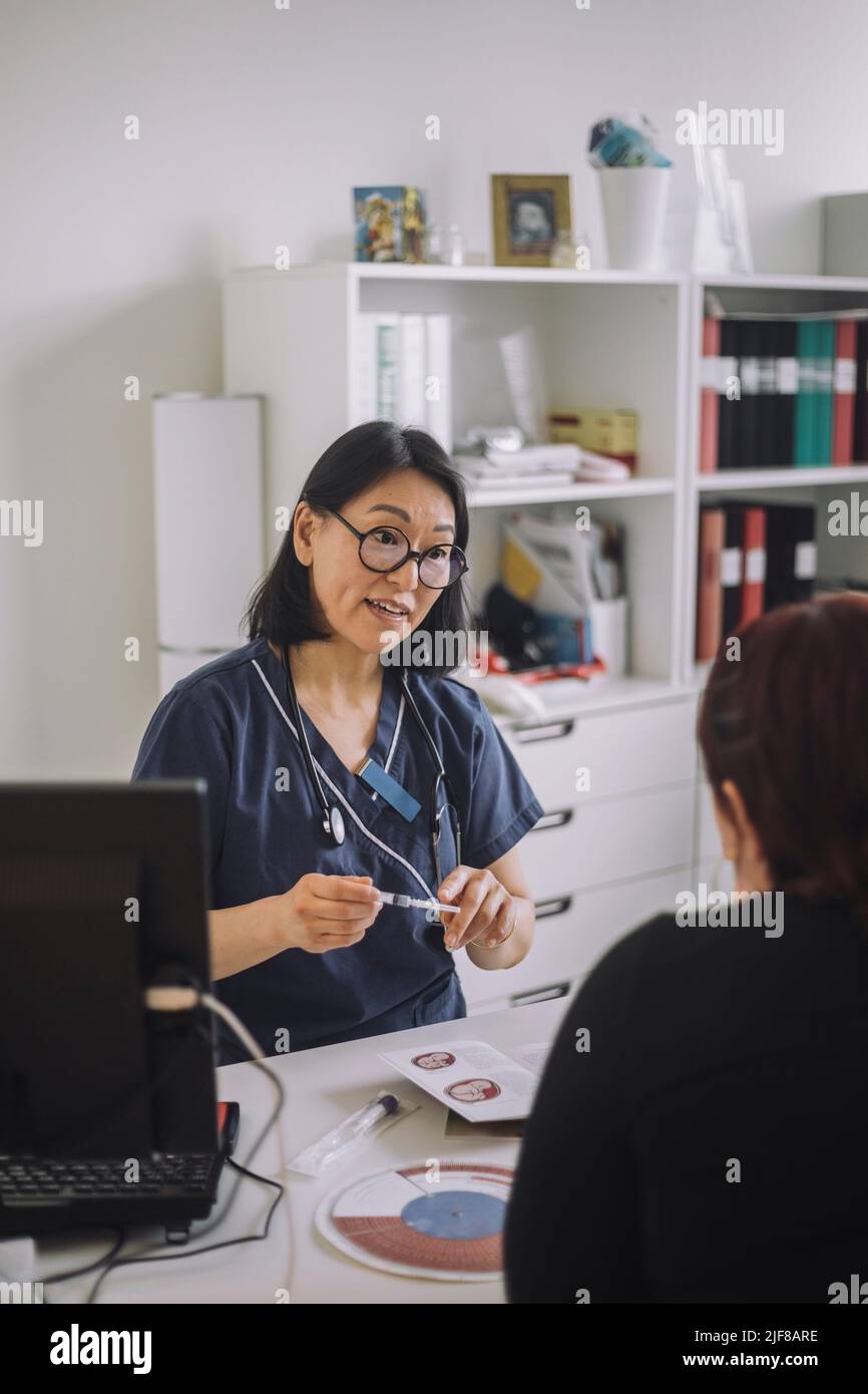 Female doctor explaining IVF syringe to young patient while sitting at ...