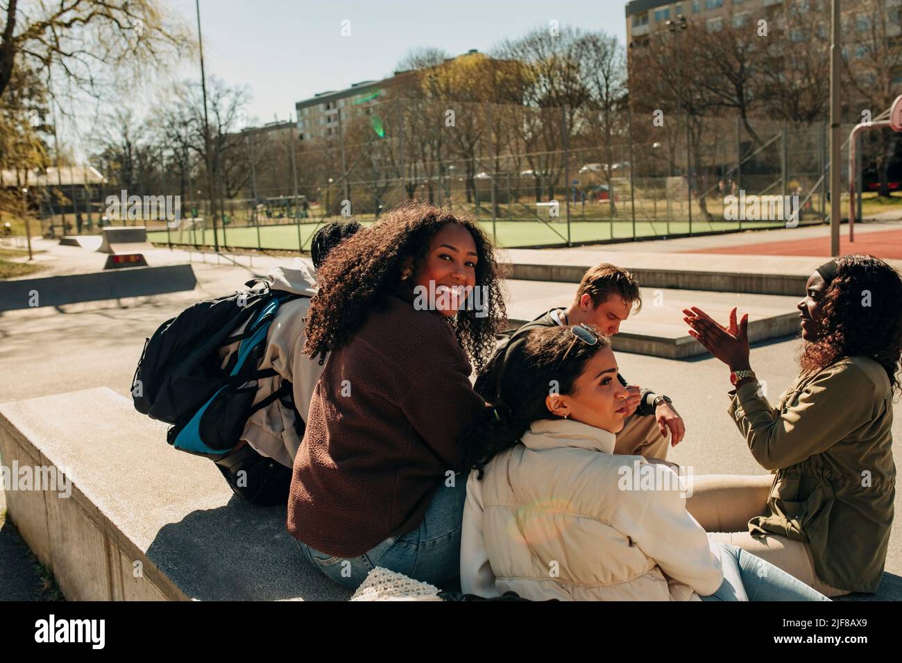 Smiling girl looking over shoulder while sitting with friends on ...