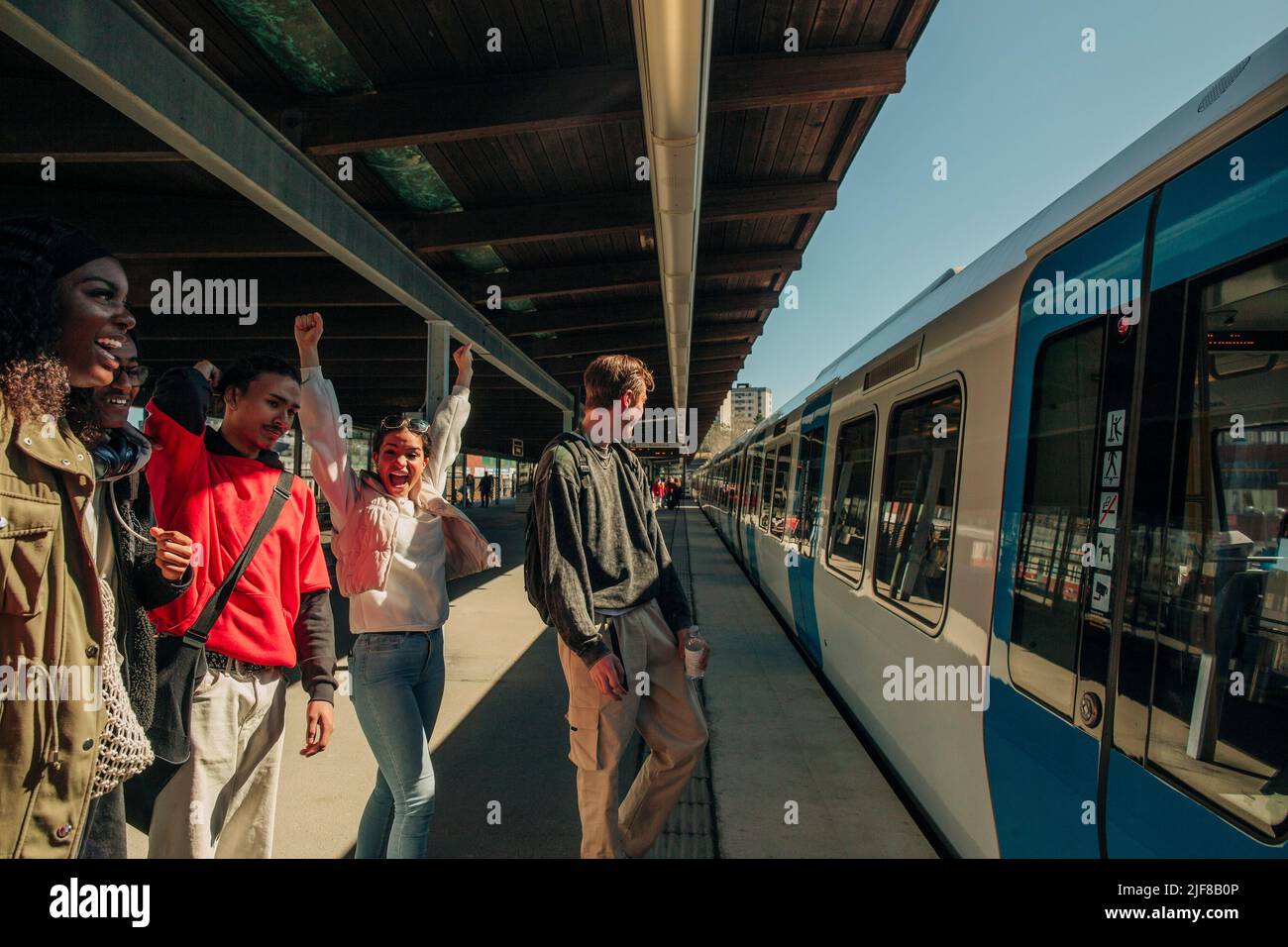 Happy multiracial friends cheering up on arrival of train at railroad ...