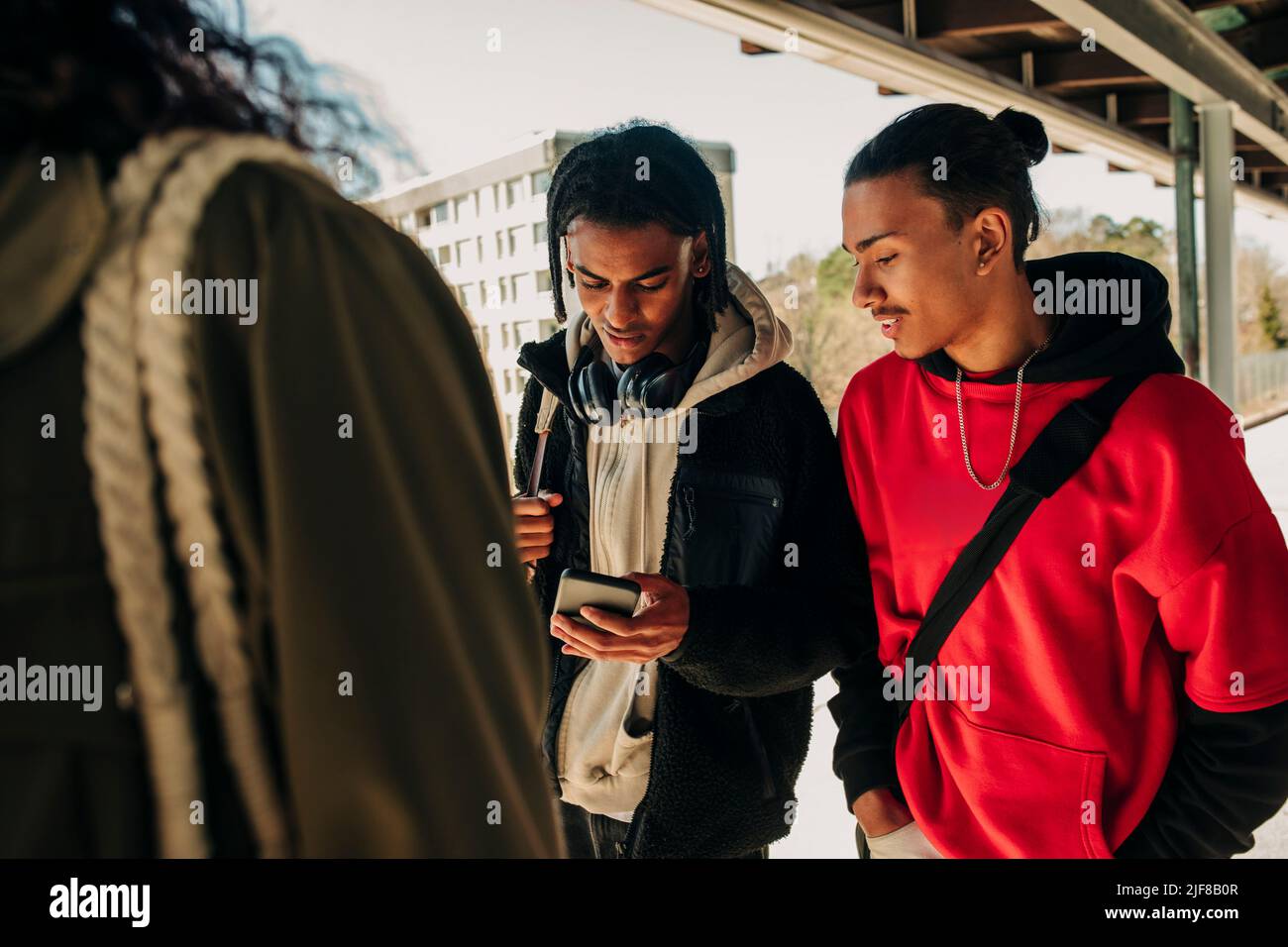 Young man sharing smart phone with friend while walking at railroad ...