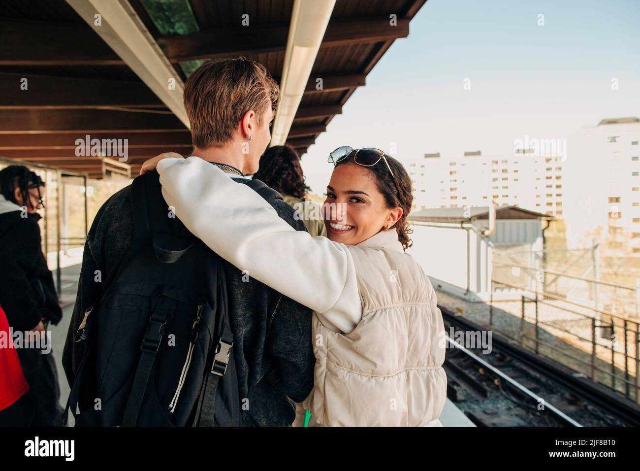Portrait of smiling woman with arm around friend walking on railroad ...