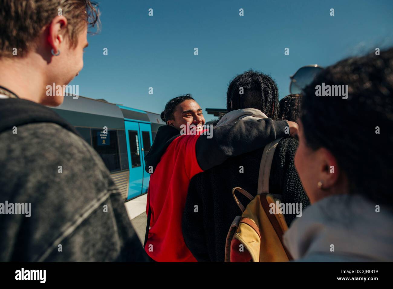 Smiling man looking over shoulder with arm around friend at railroad ...