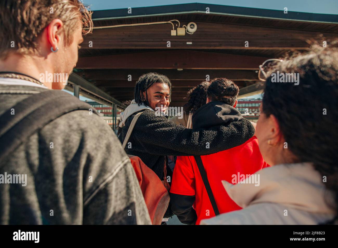 Smiling young man looking over shoulder while walking with friends at ...