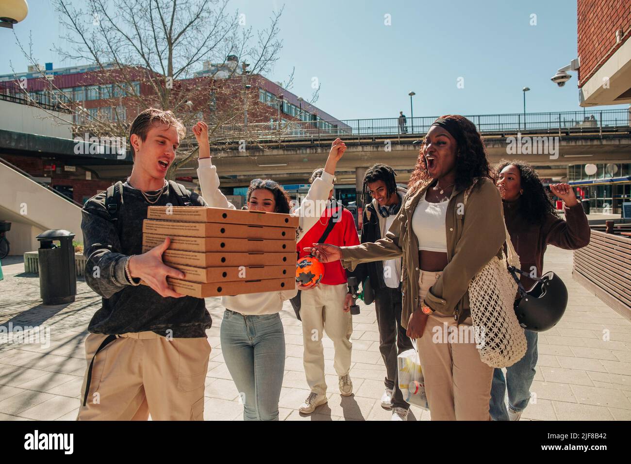 Man carrying stack of pizza boxes while walking with friends at street ...