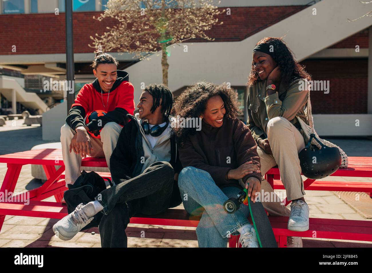 Happy multiracial young friends talking while sitting on bench Stock Photo - Alamy