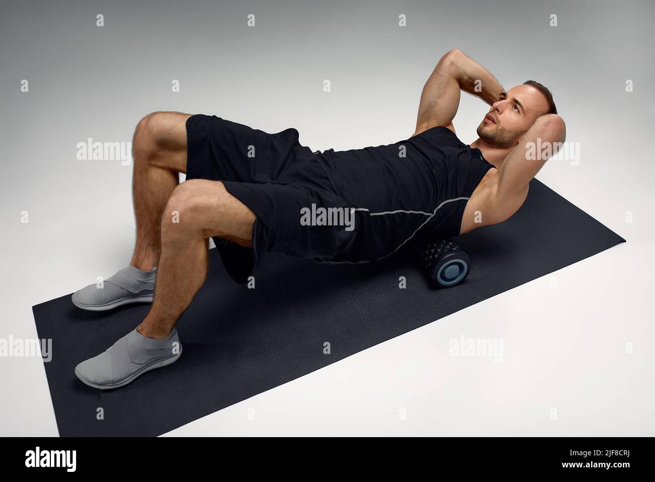 Athletic man using a foam roller to relieve sore muscles after a ...