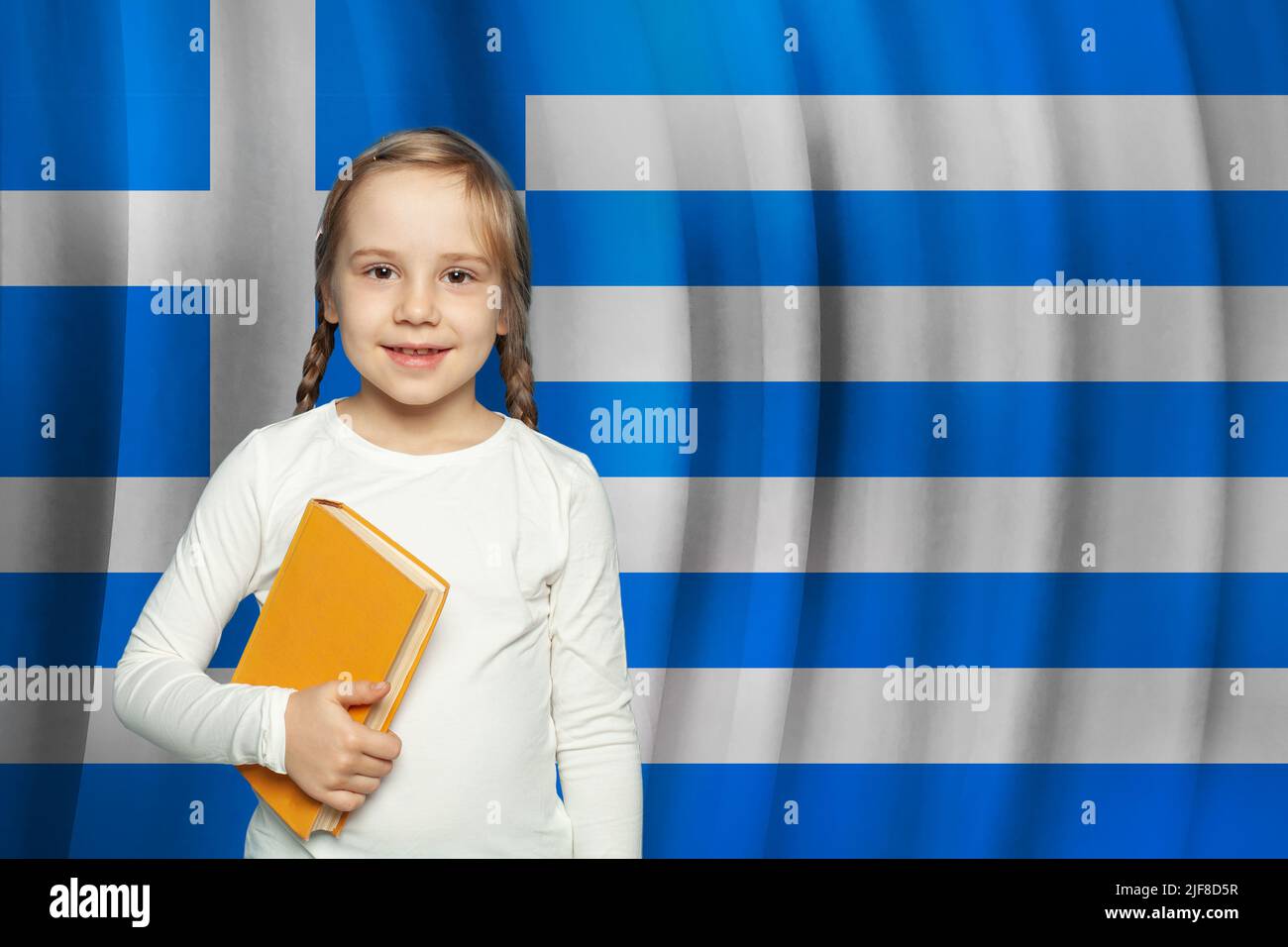 Cute Greek small girl child with book against flag of Greece background ...
