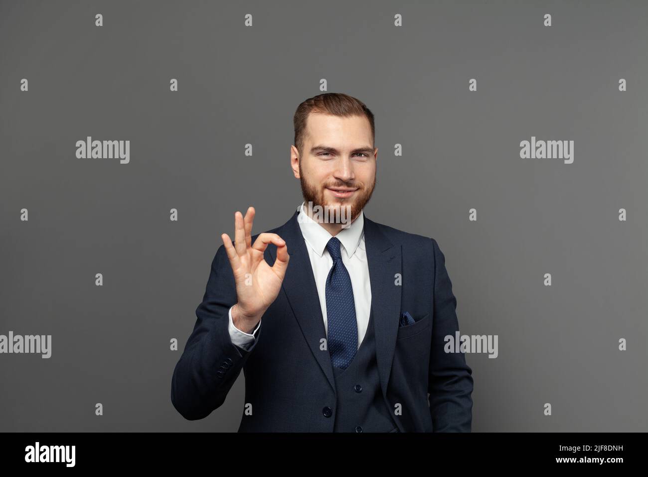 Happy young businessman showing ok sign over grey background Stock ...