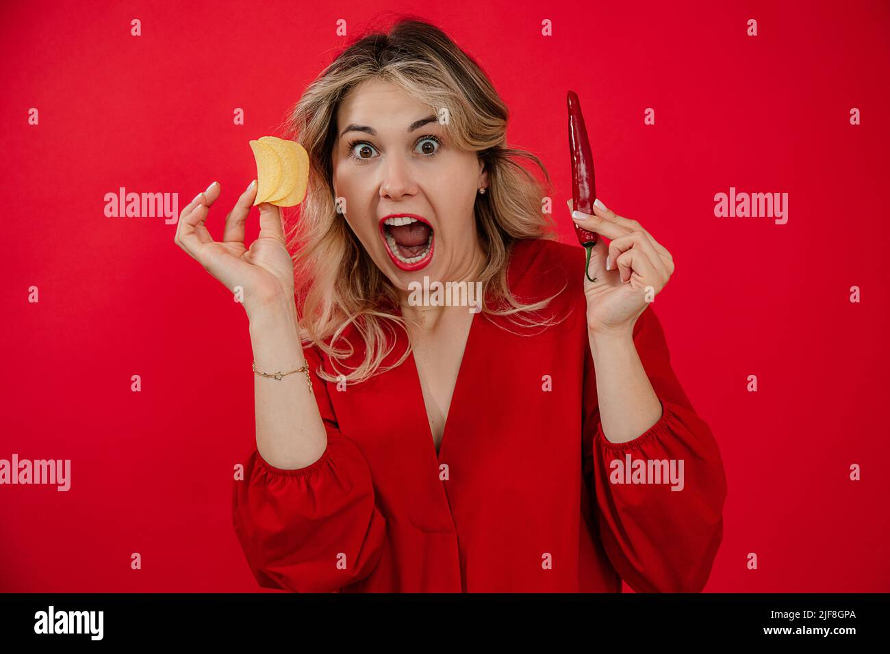 Woman in red dress on red background screams loudly and holds chili ...