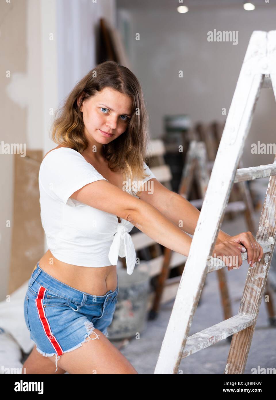 Pretty young landlady in a white blouse and short shorts poses ...