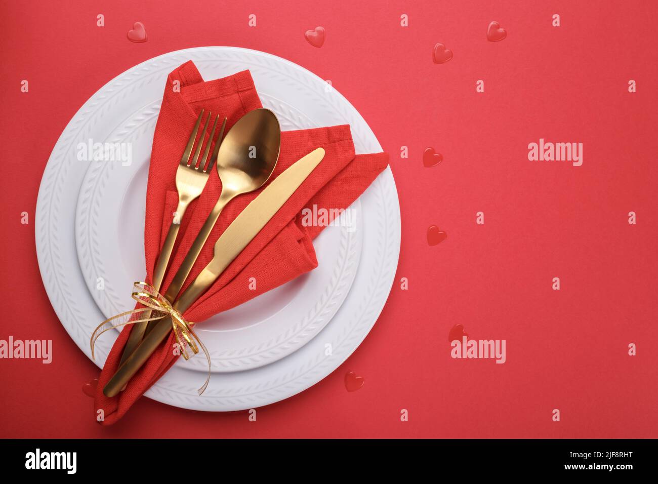 Romantic table setting, gold cutlery on the red table cloth. Valentine ...
