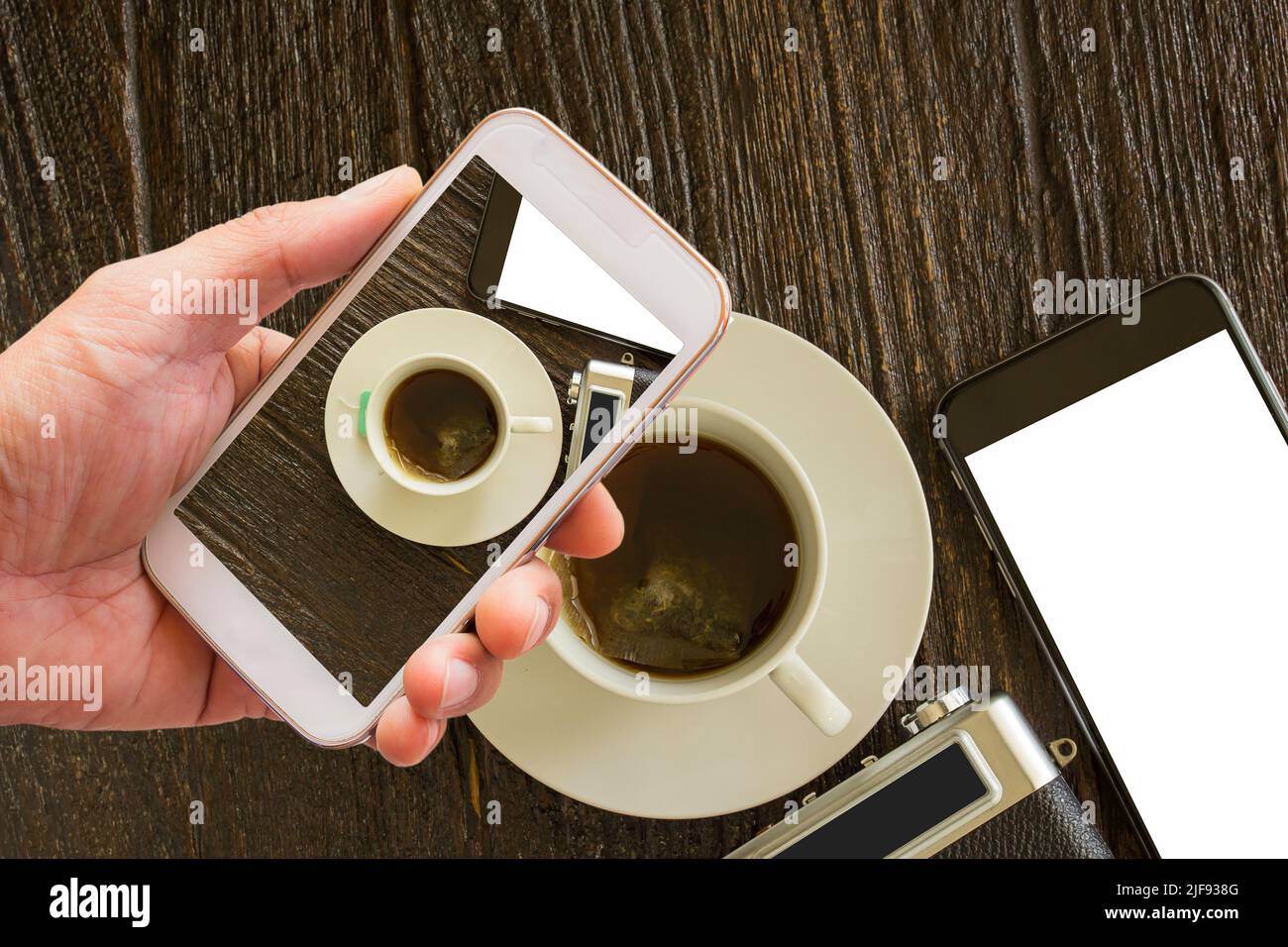 Han holding smart phone shoot a hot tea and camera on wooden table ...