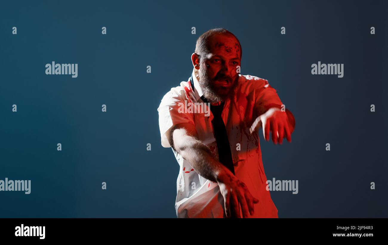 Creepy zombie growling at camera while standing on blue background ...