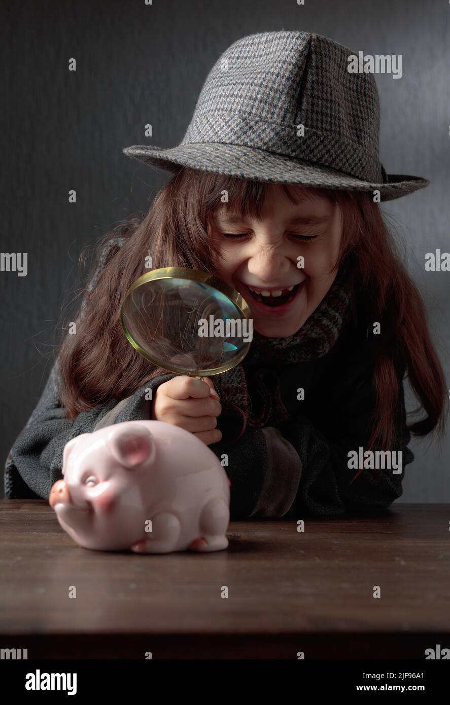 The cute little detective with a magnifying glass looks at the piggy ...