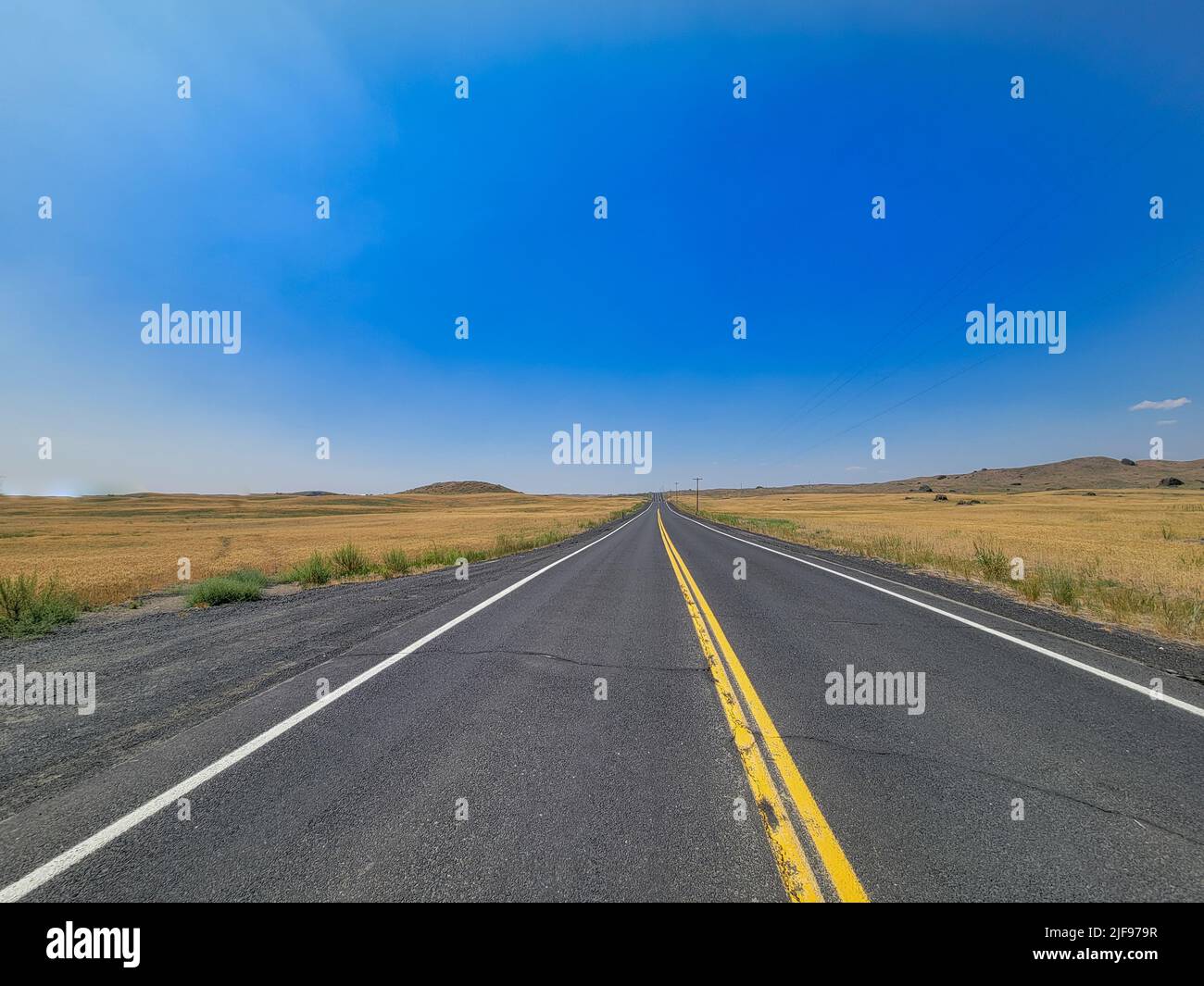A long empty asphalt highway through open fields in Washington state on ...