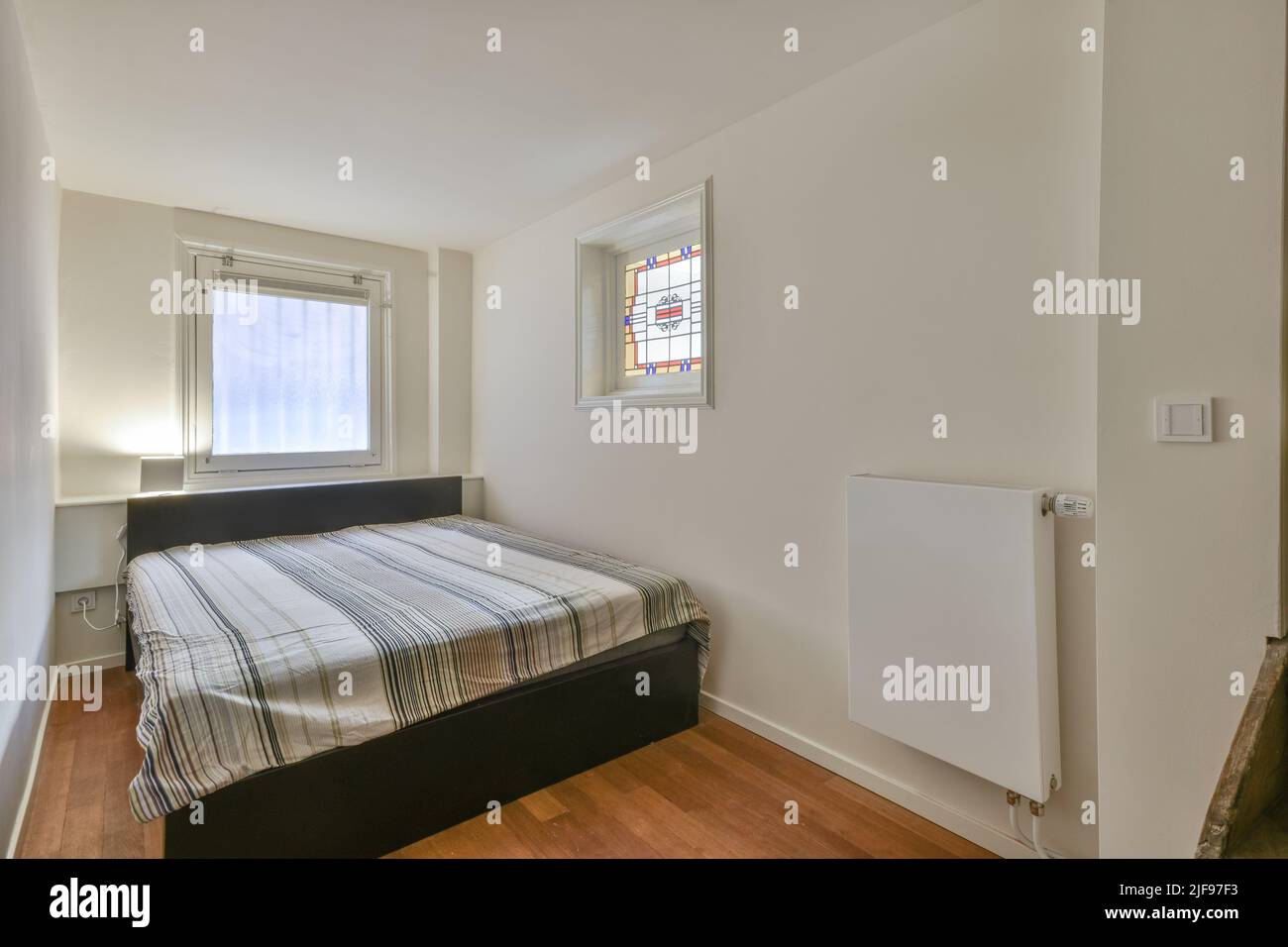 Spacious bright bedroom with a white stylish radiator and parquet floor ...