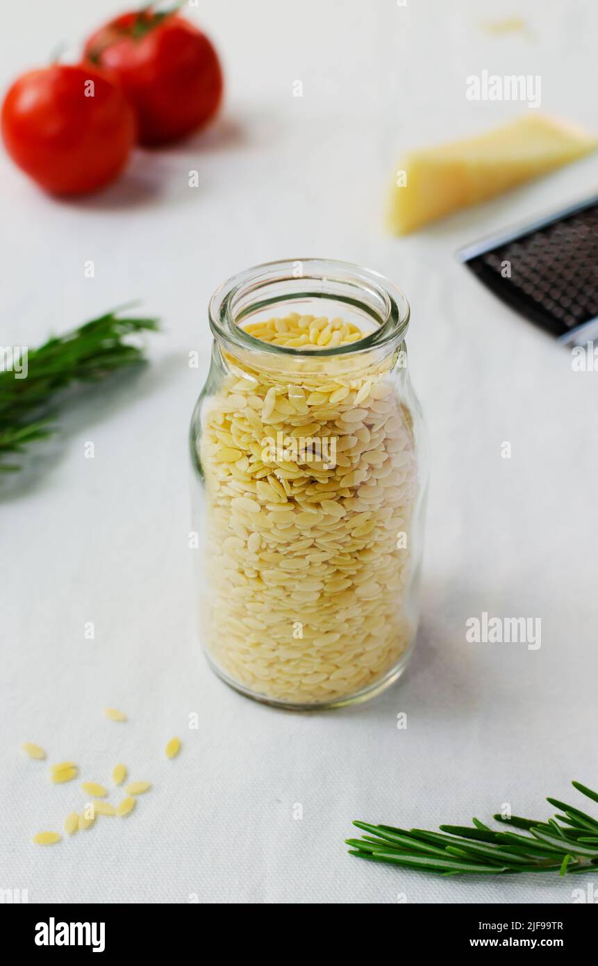Raw Italian risoni pasta in a glass jar with ingredients on a table ...